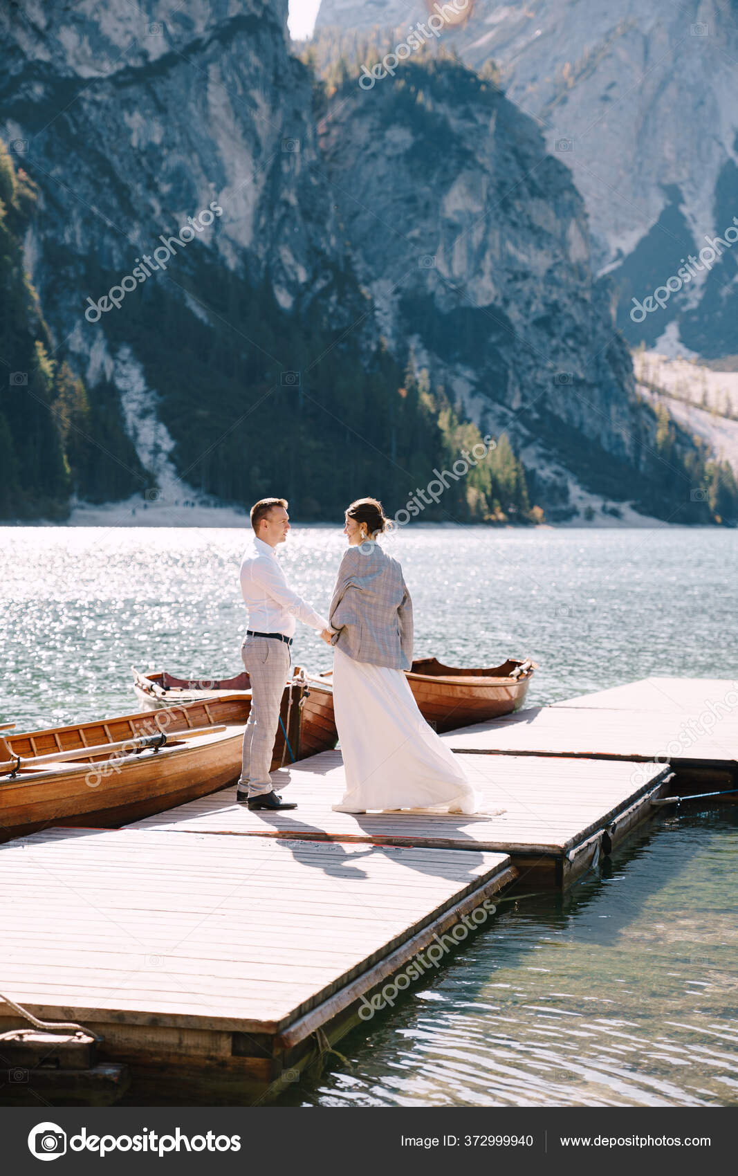 The bride and groom walk along a wooden boat dock at the Lago di Braies ...