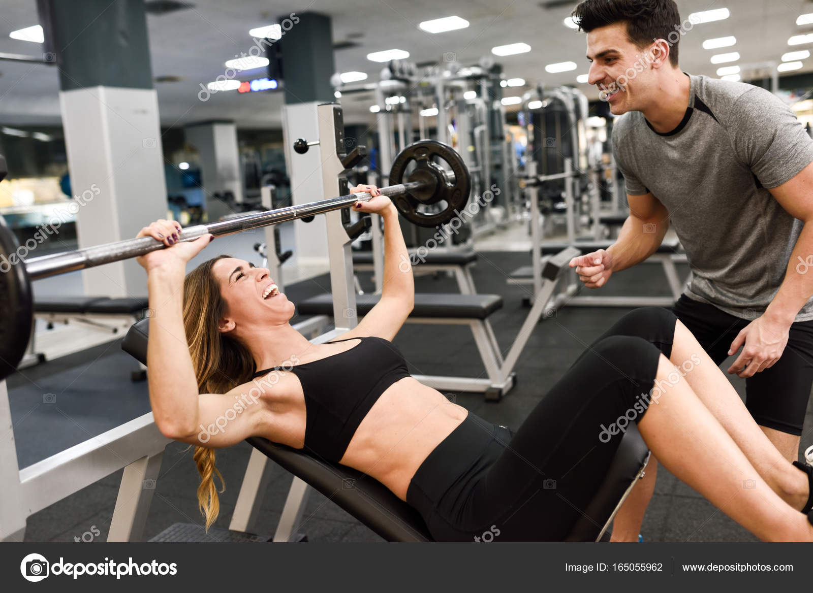 Personal trainer helping a young woman lift weights Stock Photo by ...