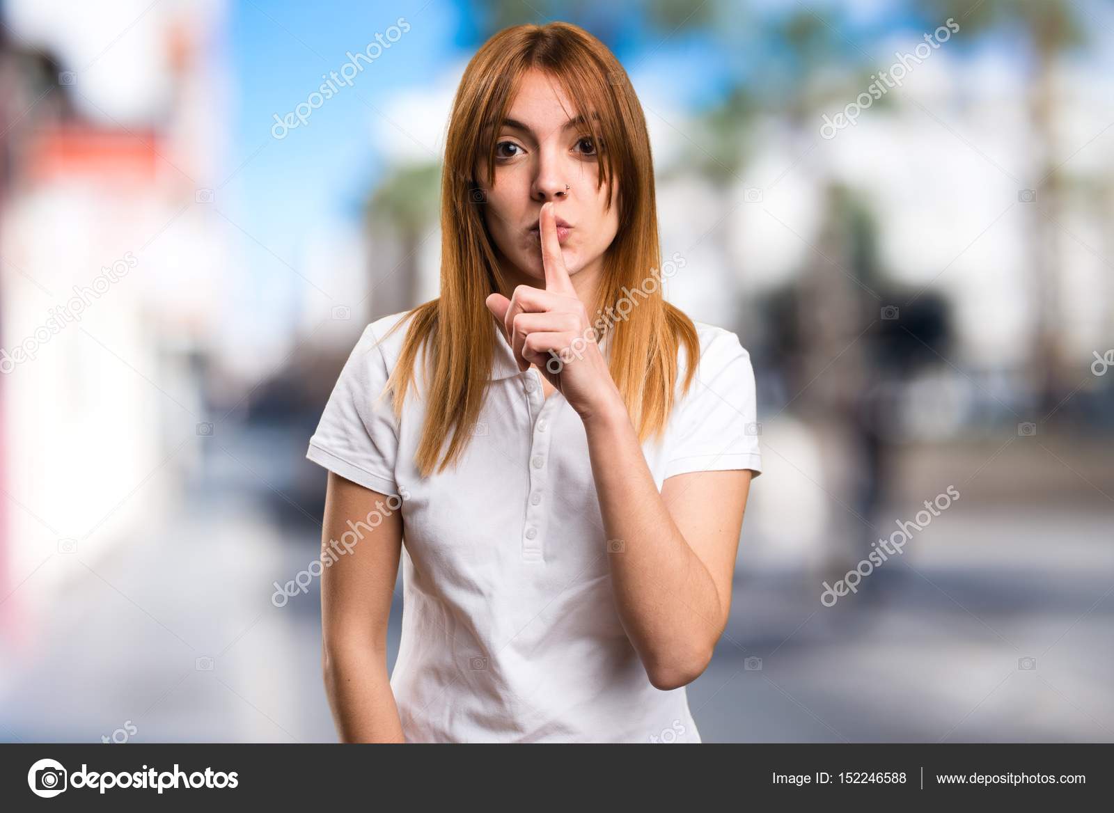 Beautiful young girl making silence gesture on unfocused background ...