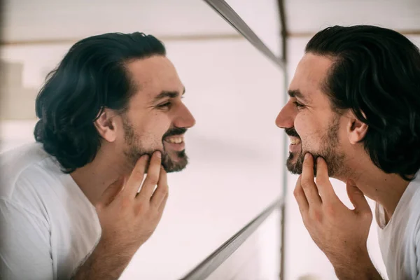 A handsome man looks in the mirror. Men's personal care. A young guy ...