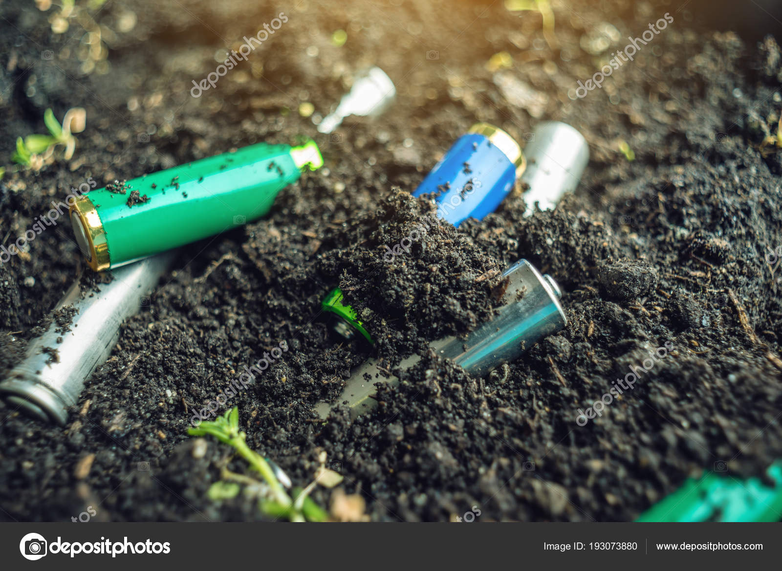 Used alkaline batteries lie in the soil where plants grow. Concept of ...