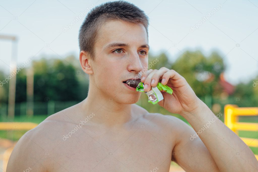 Man is eating carbohydrate bar during workout. Outdoor gym backg Stock ...