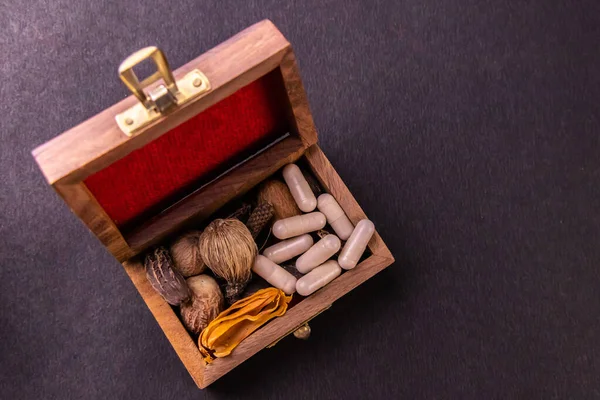 Dried herbs, spices and herbal capsules in a wooden box on black ...