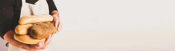Un hombre en un delantal sostiene varios panes frescos con pan ...