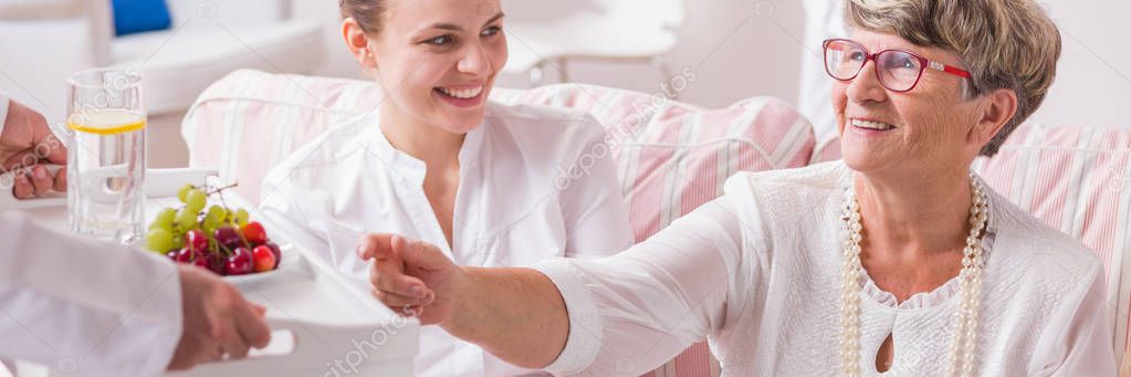 Nurse holding tray with glass of water and fruits for senior woman ...