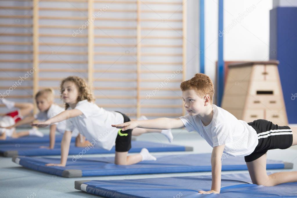 Grupo de niños haciendo gimnasia en alfombras azules durante la clase ...
