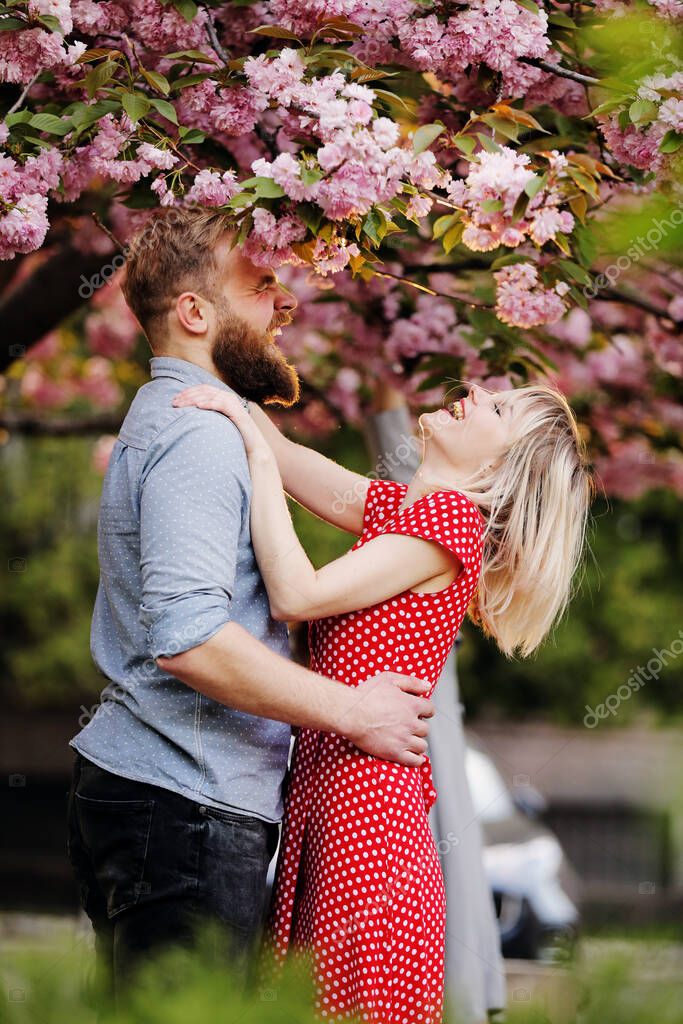 Elegante pareja cerca del rbol Sakura. hermosa pareja joven, hombre con barba y mujer rubia ...