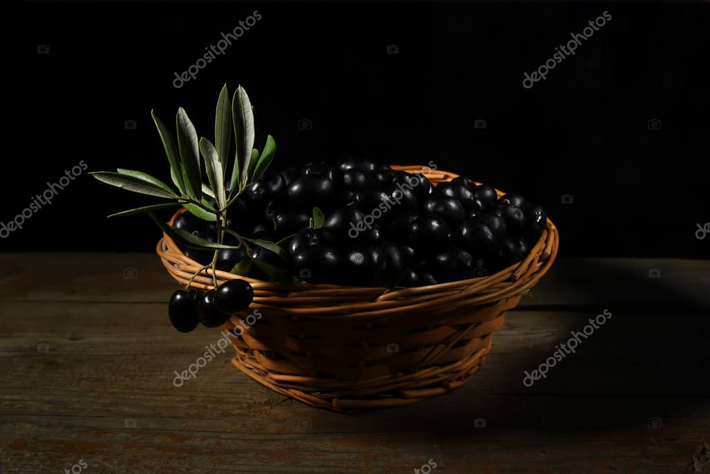 Una cesta wiker llena de aceitunas negras maduras y frescas de Puglia ...