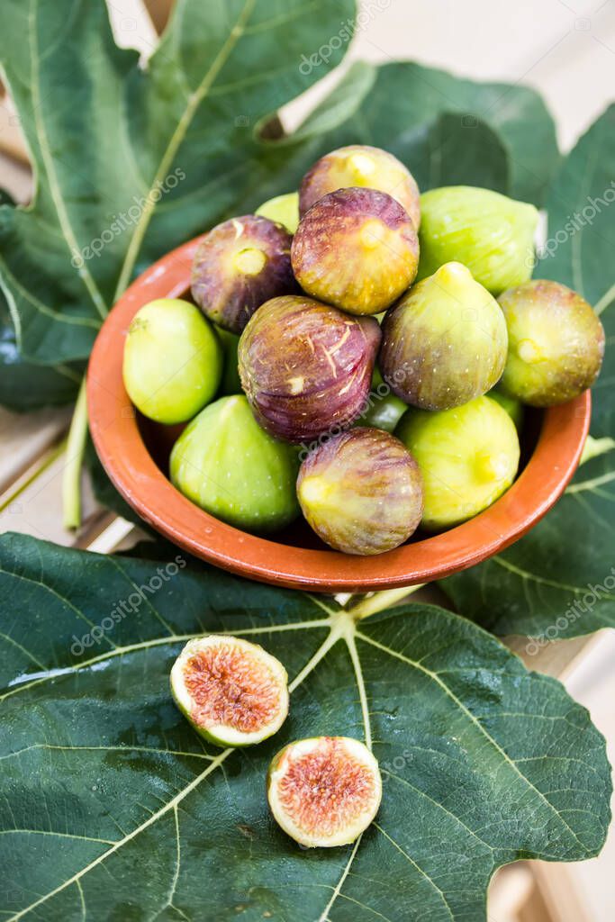 Higos frescos en un tazón de barro sobre hojas verdes, verticales 2022