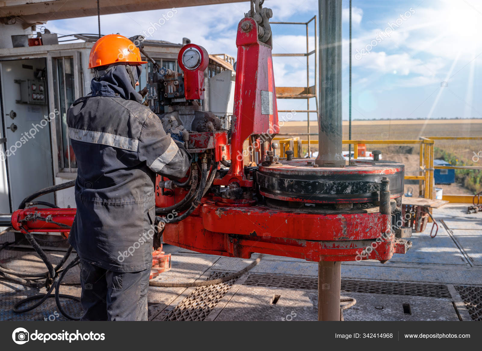 Work driller in red uniform, in helmet and goggles. He uses a hydraulic ...