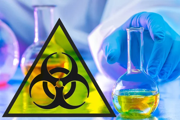 Chemist's hands and a test tube on the background of a biohazard sign ...