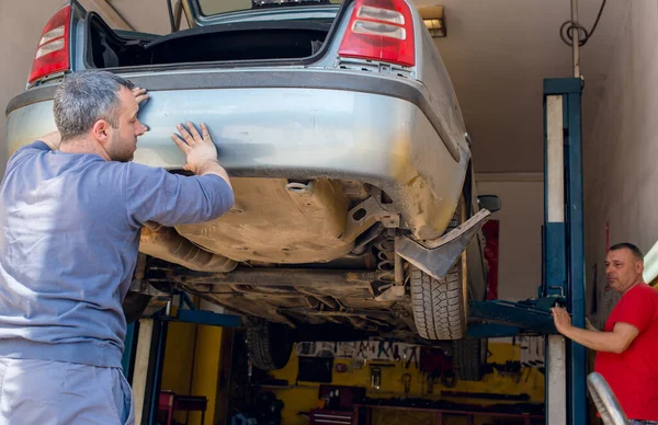 Car mechanics working on the back of the car. Car is lifted with ...