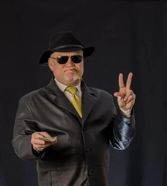 A man in black clothes, a black leather coat, hat. Ganster with a cigar ...