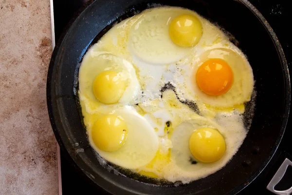 Bright orange egg yolk in a frying pan on a black skillet while ...