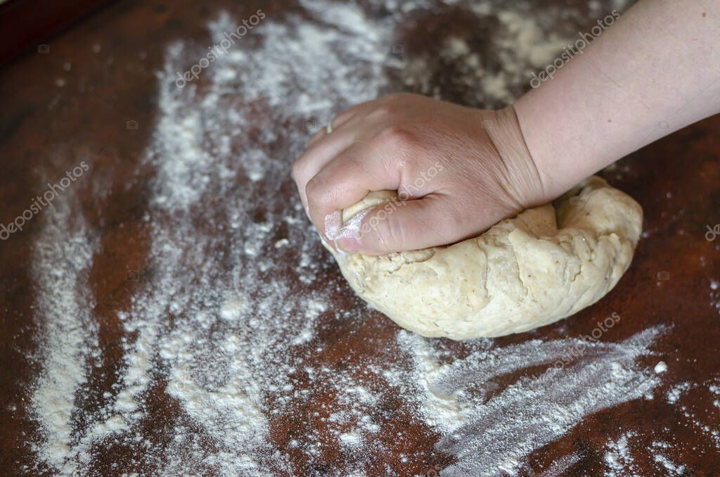 La mano femenina amasa un pedazo de masa en la mesa de la cocina. La ...