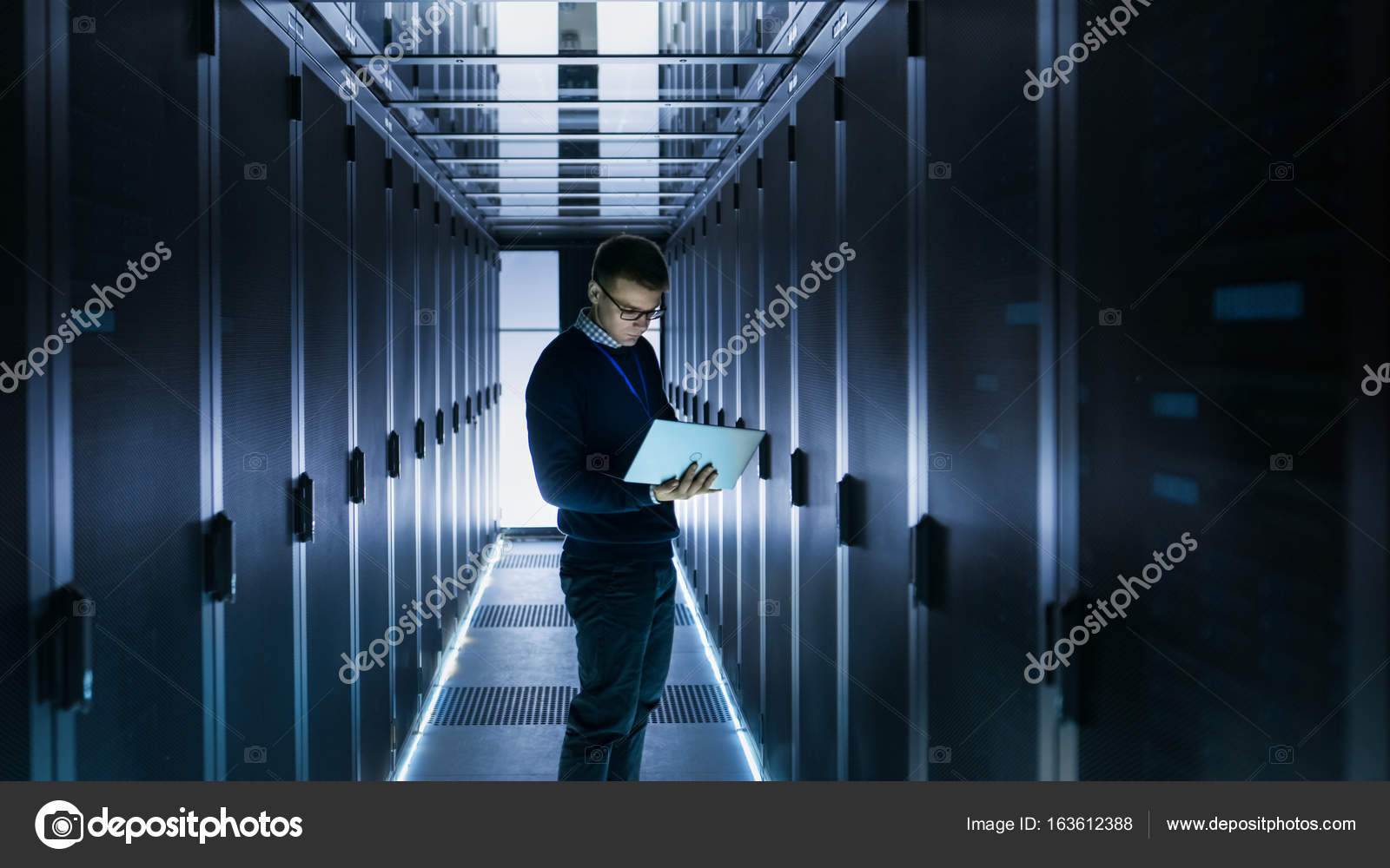 Male IT Engineer Works on a Laptop in front of Server Cabinet at ...