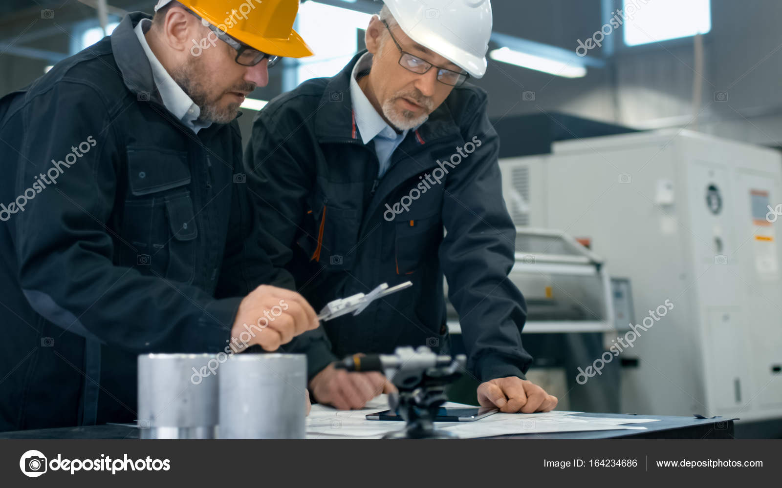Two engineers discuss a blueprint while checking information on Stock ...