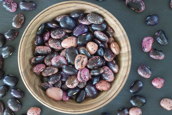 grain purple beans of different colors in a wooden bowl on a black ...