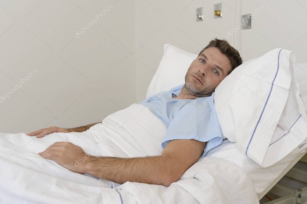 Young patient man lying at hospital bed resting tired looking sad and ...
