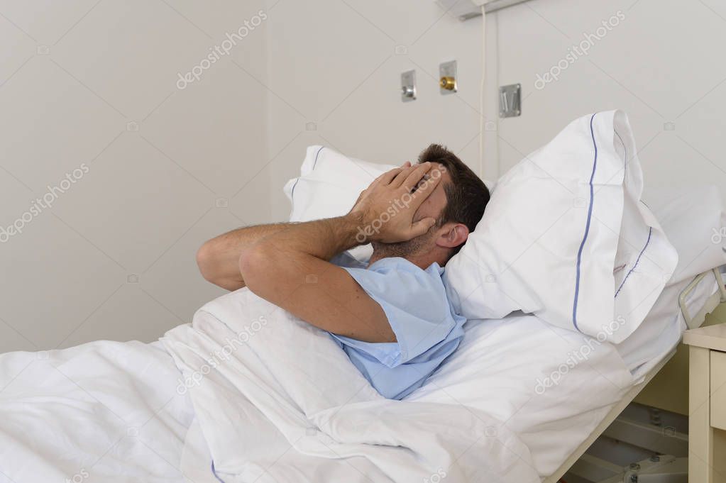 Young patient man lying at hospital bed resting tired looking sad and ...