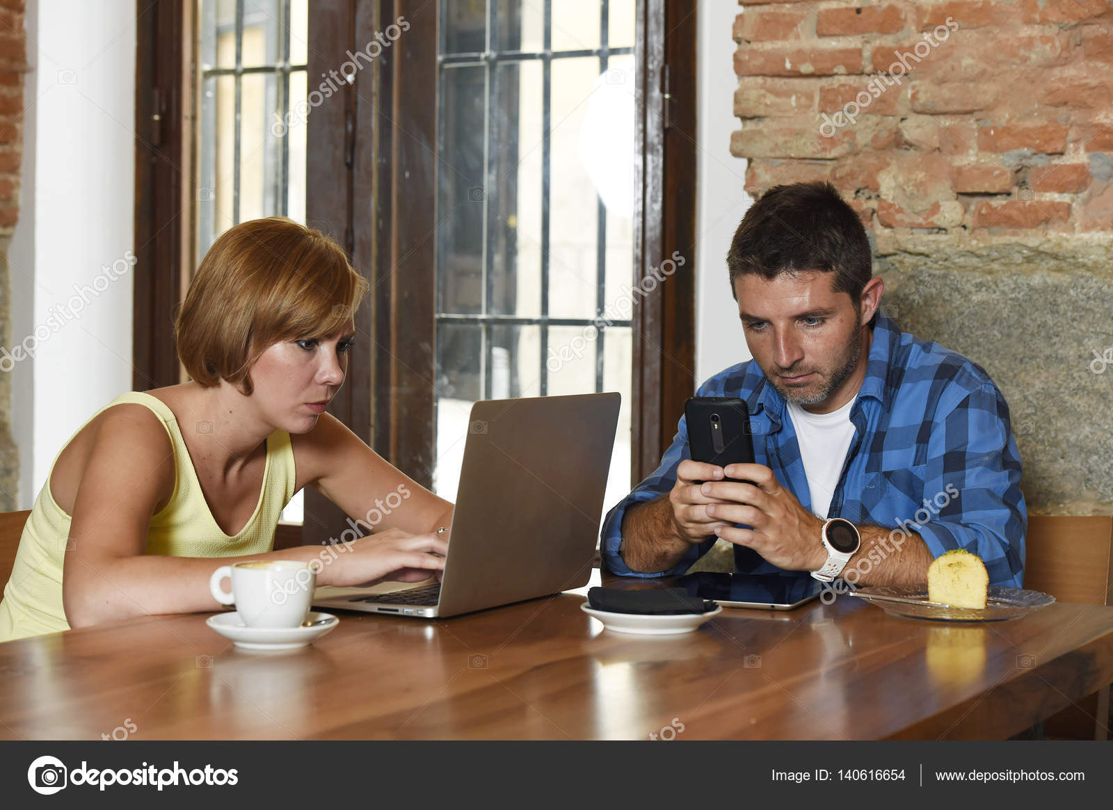 Couple using laptop computer and mobile phone networking ignoring each ...