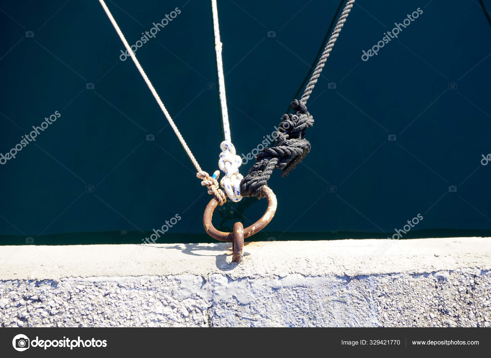 Ropes tied to knots and tethered to a metal hoop on a stone waterfront ...