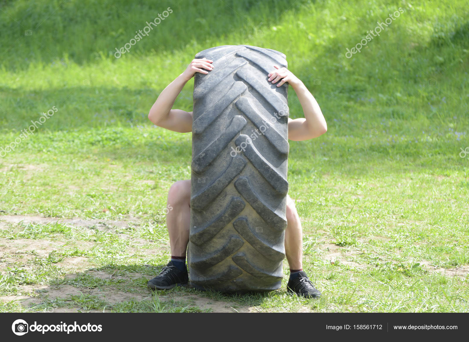 Man sits in big tractor tire on green grass background — Stock Photo ...