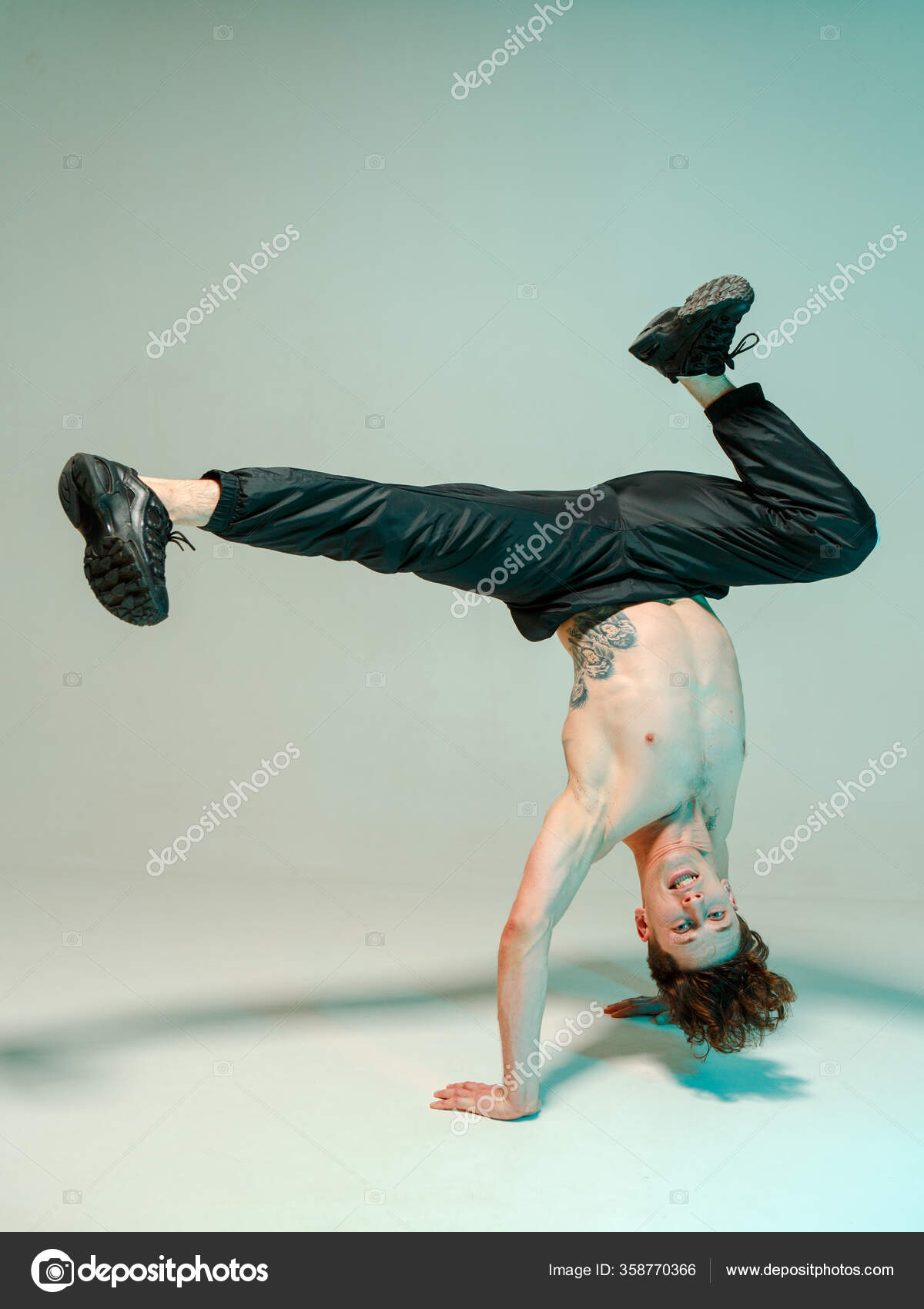 A young graceful guy is dancing a break dance on the floor without a t ...