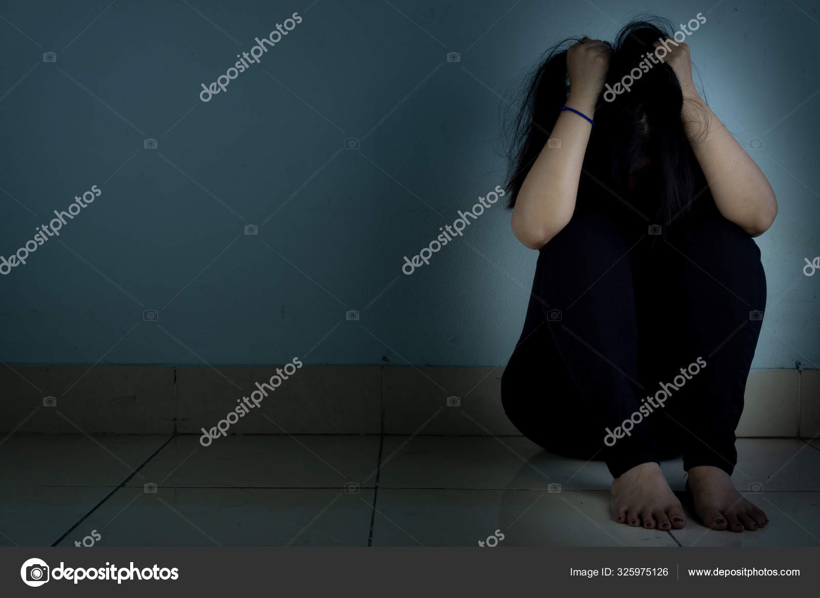 Sad woman hug her knee and cry sitting alone in a dark room. Dep ...
