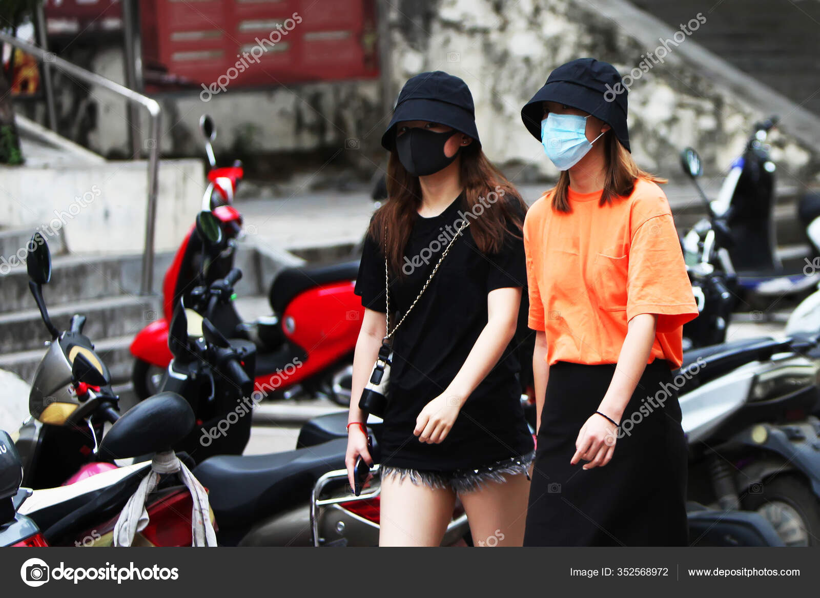 Two Chinese women are walking down the street with gauze masks on their ...