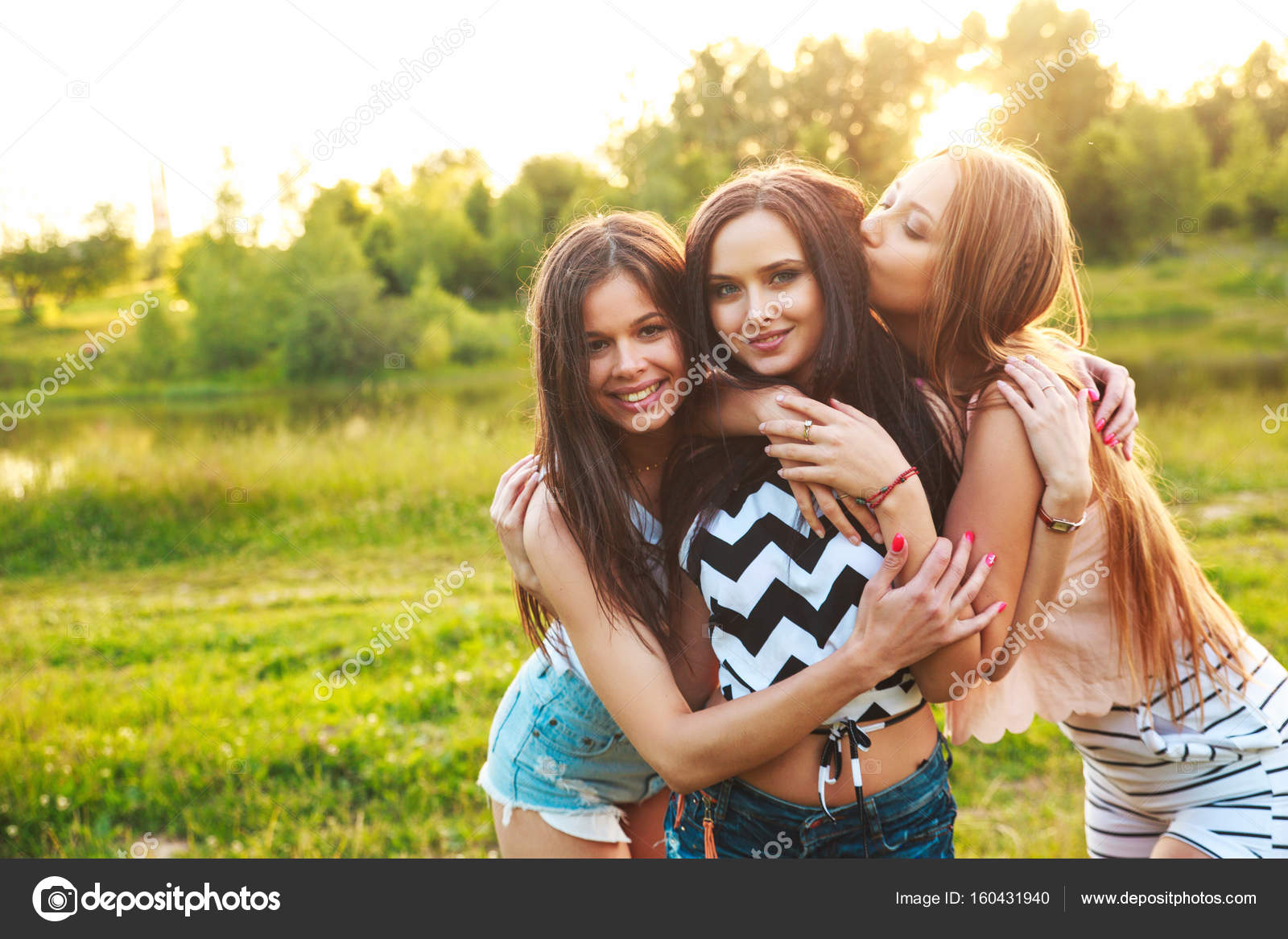 Three women hugging each other outdoors and laughing on sunset. Stock ...