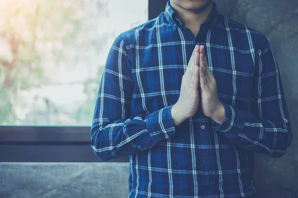 A young man raises hands up praying to God over concrete wall against ...