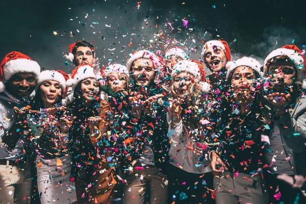 People in Santa hats blowing confetti - Stock Image - Everypixel