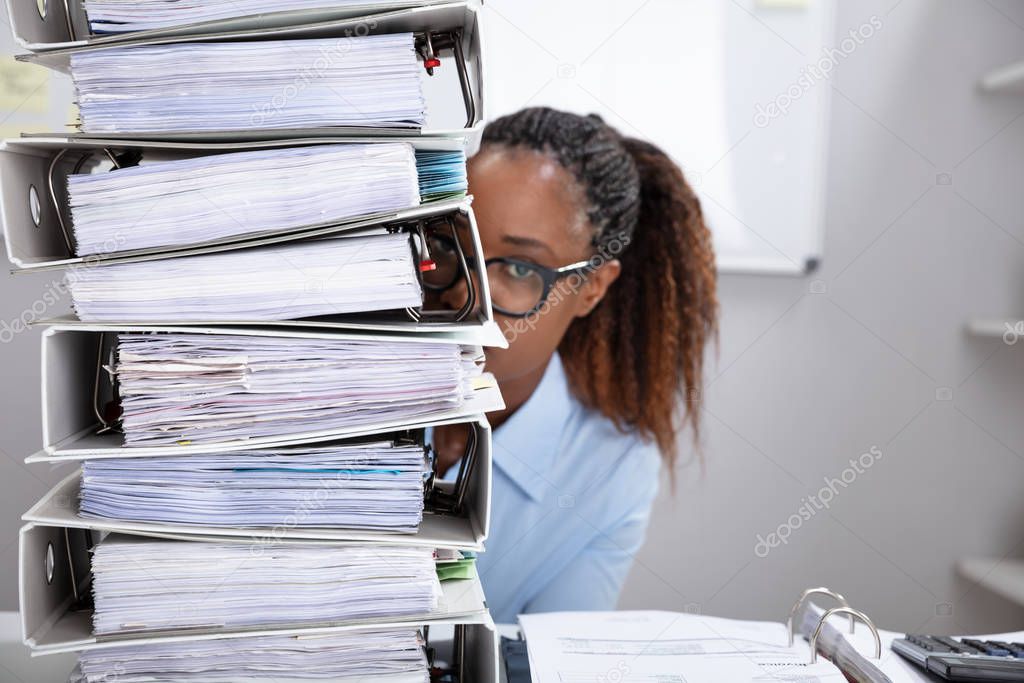 Primer plano de una mujer de negocios escondiéndose detrás de la pila de carpetas en el ...