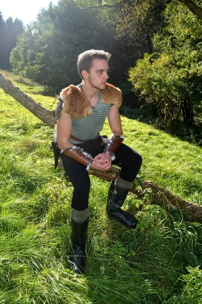 young medieval archer with chain mail sits on tree branch in nature in ...