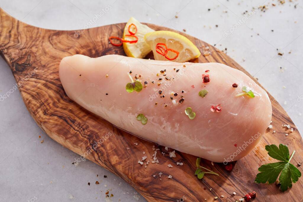 Pechuga de pollo de piel cruda con condimentos, especias y hierbas, en una tabla de madera con ...