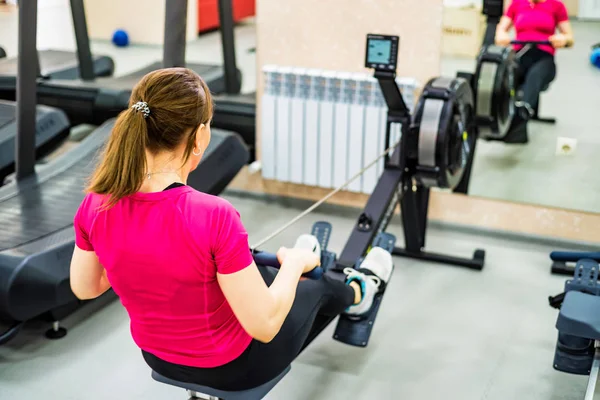 Young woman on rowing machine in gym - Stock Image - Everypixel