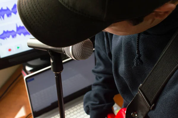 Young man with cap singing and playing electric guitar to record a song ...