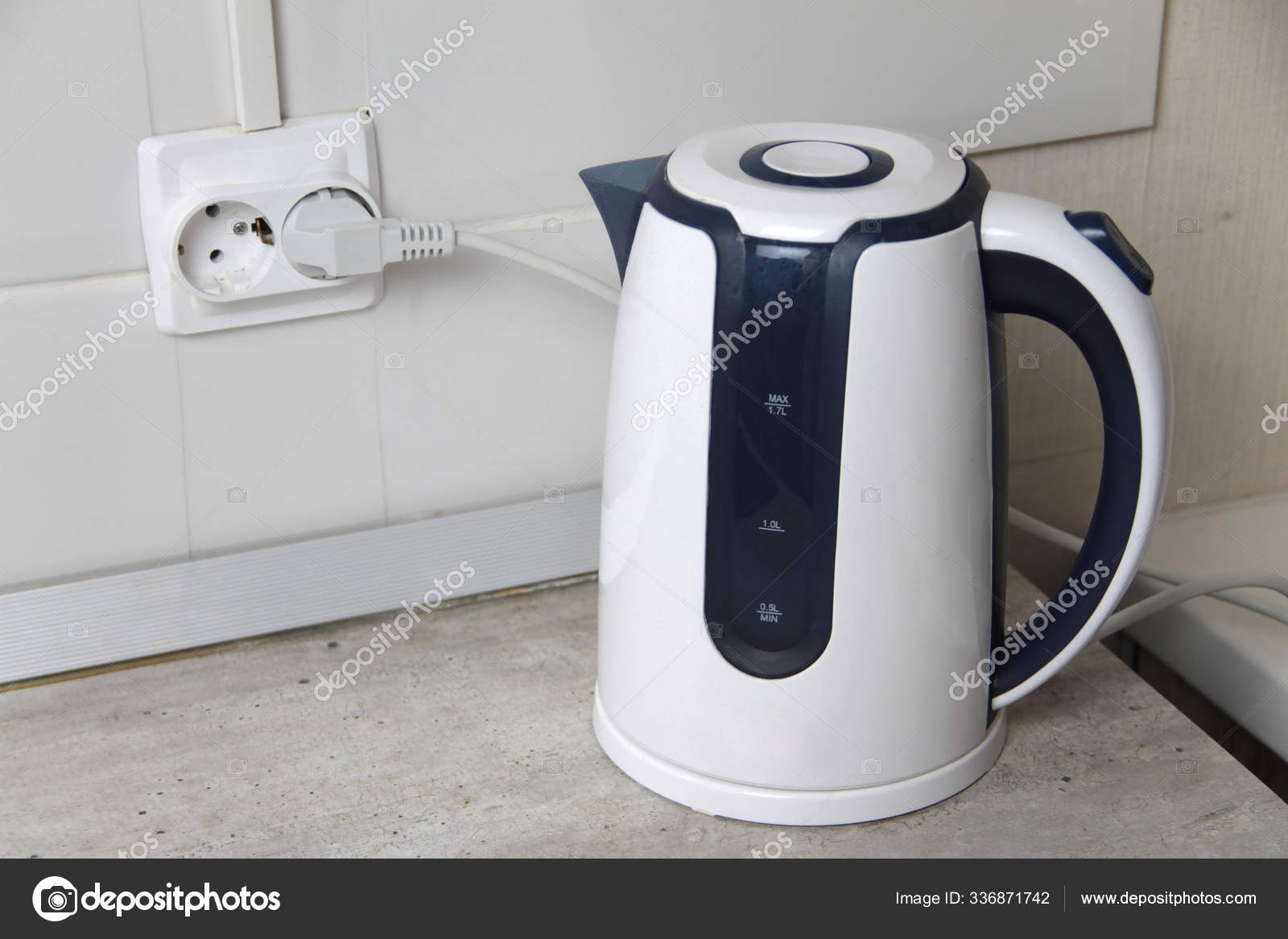 White electric kettle stands on a gray table plugged into a power ...