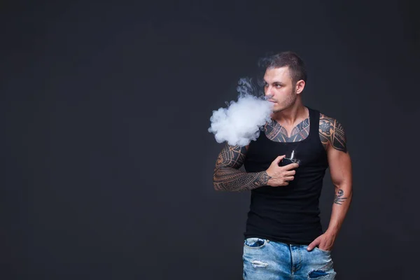 Vaper. The man with a muscular torso with tattoos smoke an electronic ...
