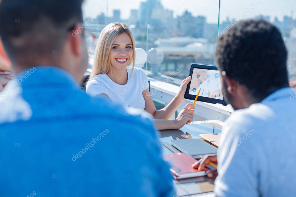 Alegre señora rubia mostrando tableta con diagramas y estadísticas 2025