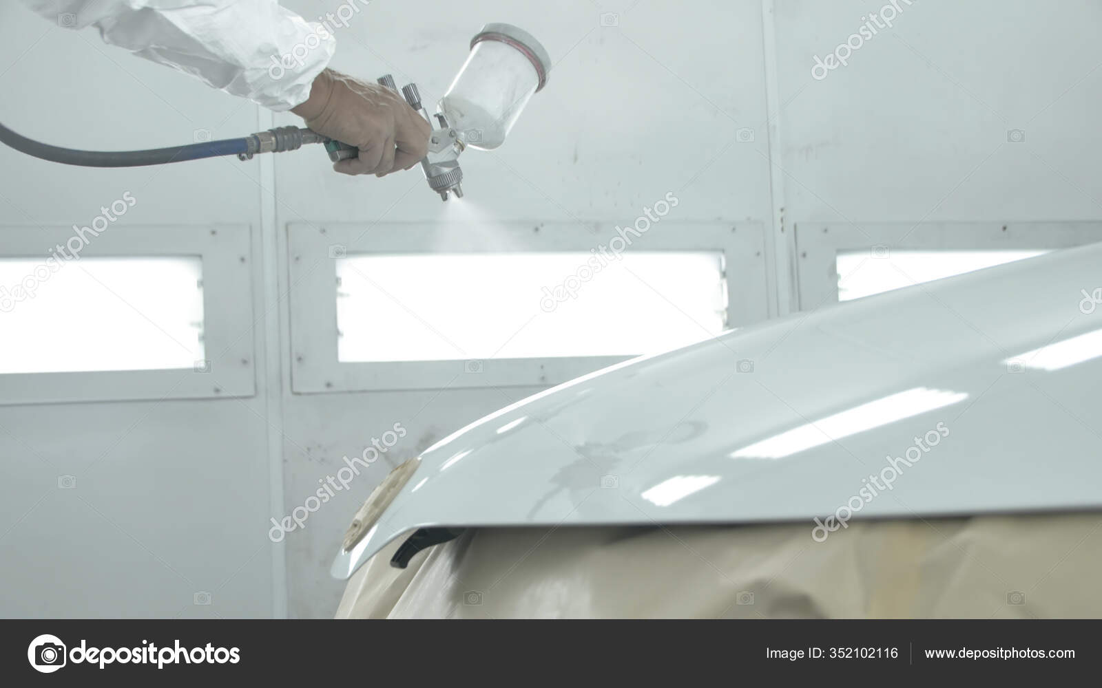 Process of painting a white car in a spray booth. Man using a spray gun ...