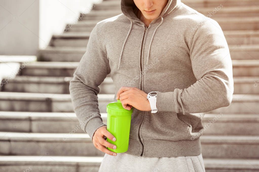 Joven hombre activo va a beber mirando su reloj, horario, al aire libre ...