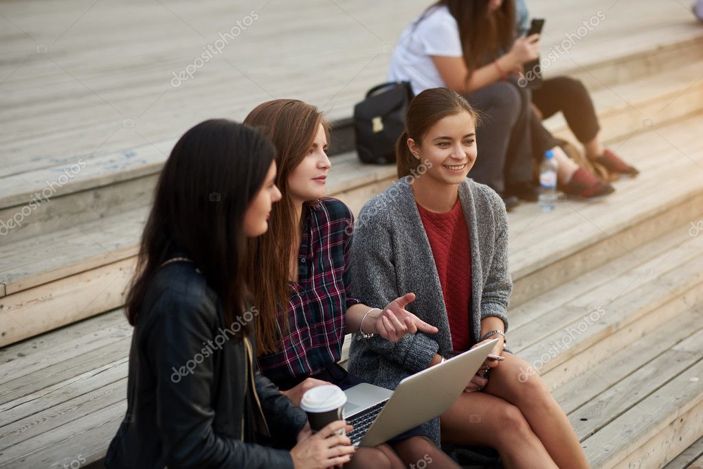 Young female students having fun conversation, while are sitting with ...