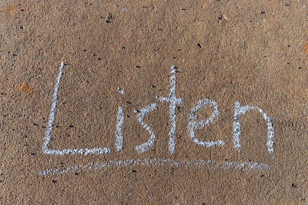 the word Listen written with sidewalk chalk on gray concrete pavement ...