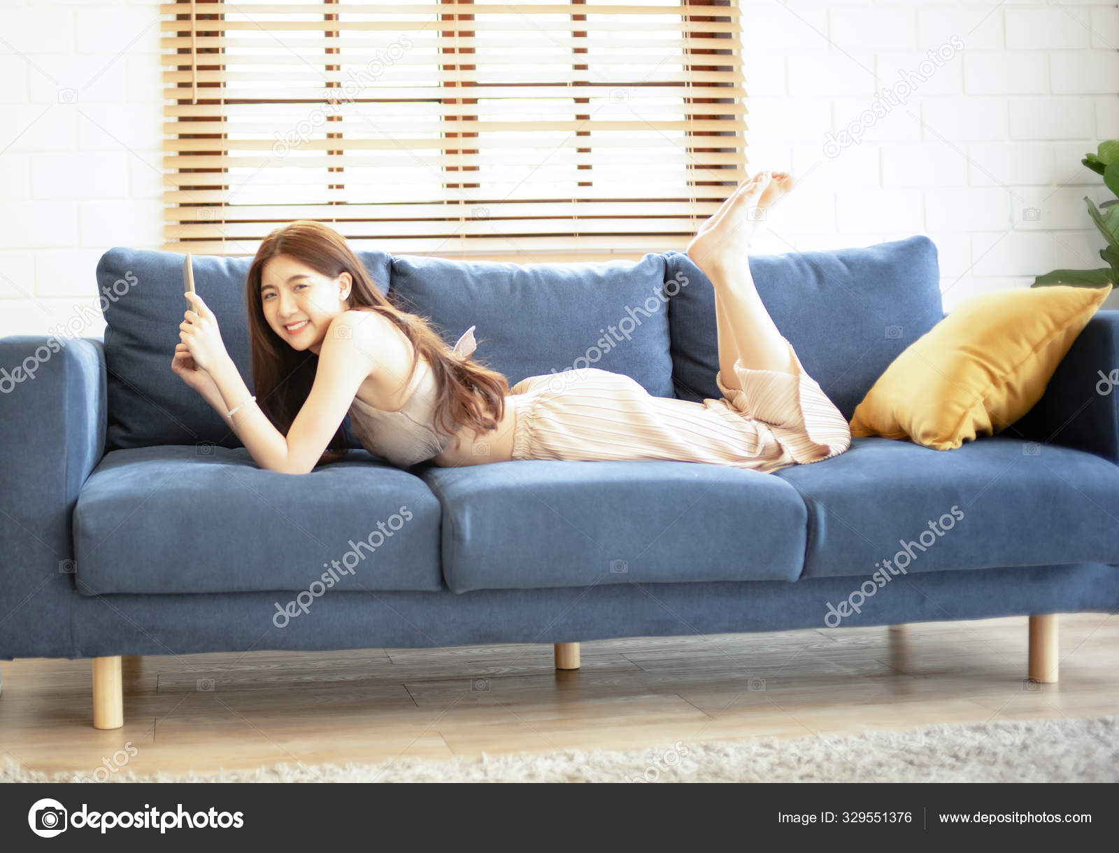 Beautiful Young Asian Woman Using Tablet Lying Down On Sofa And Stock