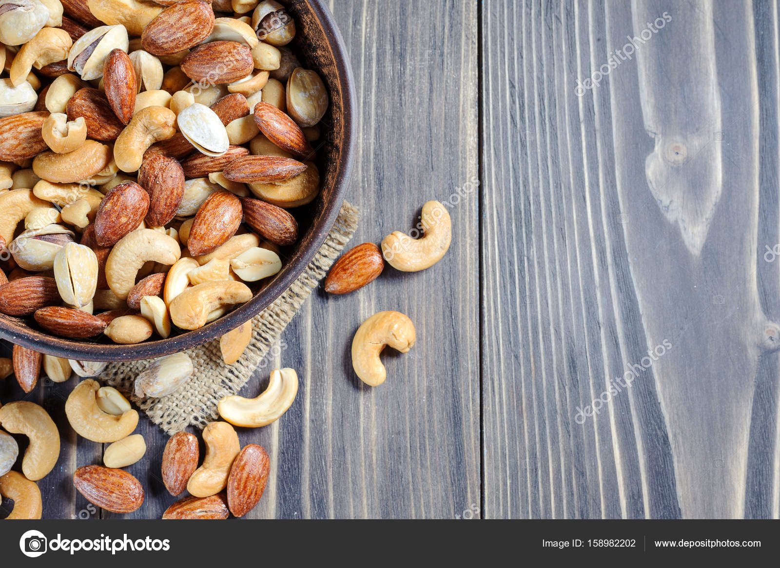 Mixed nuts spilling out of bowl on wooden table. Macro still-life with ...
