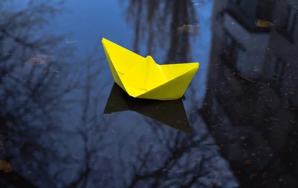 bright yellow paper boat on a background of gloomy autumn urban puddles ...