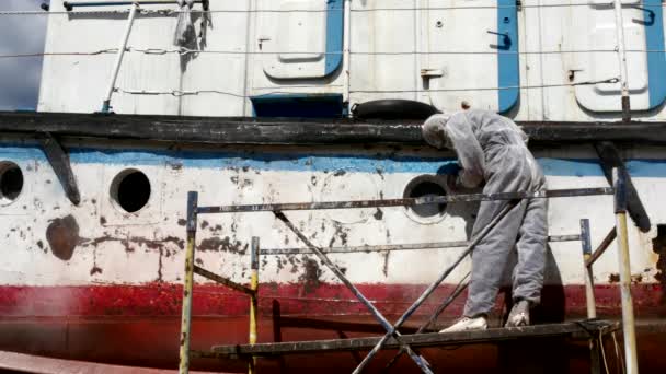 Working people tear off paint on metal in repairs process at shipyard ...