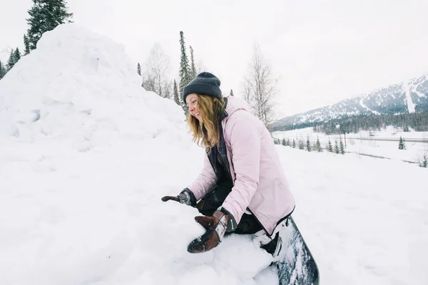Smiling Snowboarder female building kicker for jump from snow pieces ...